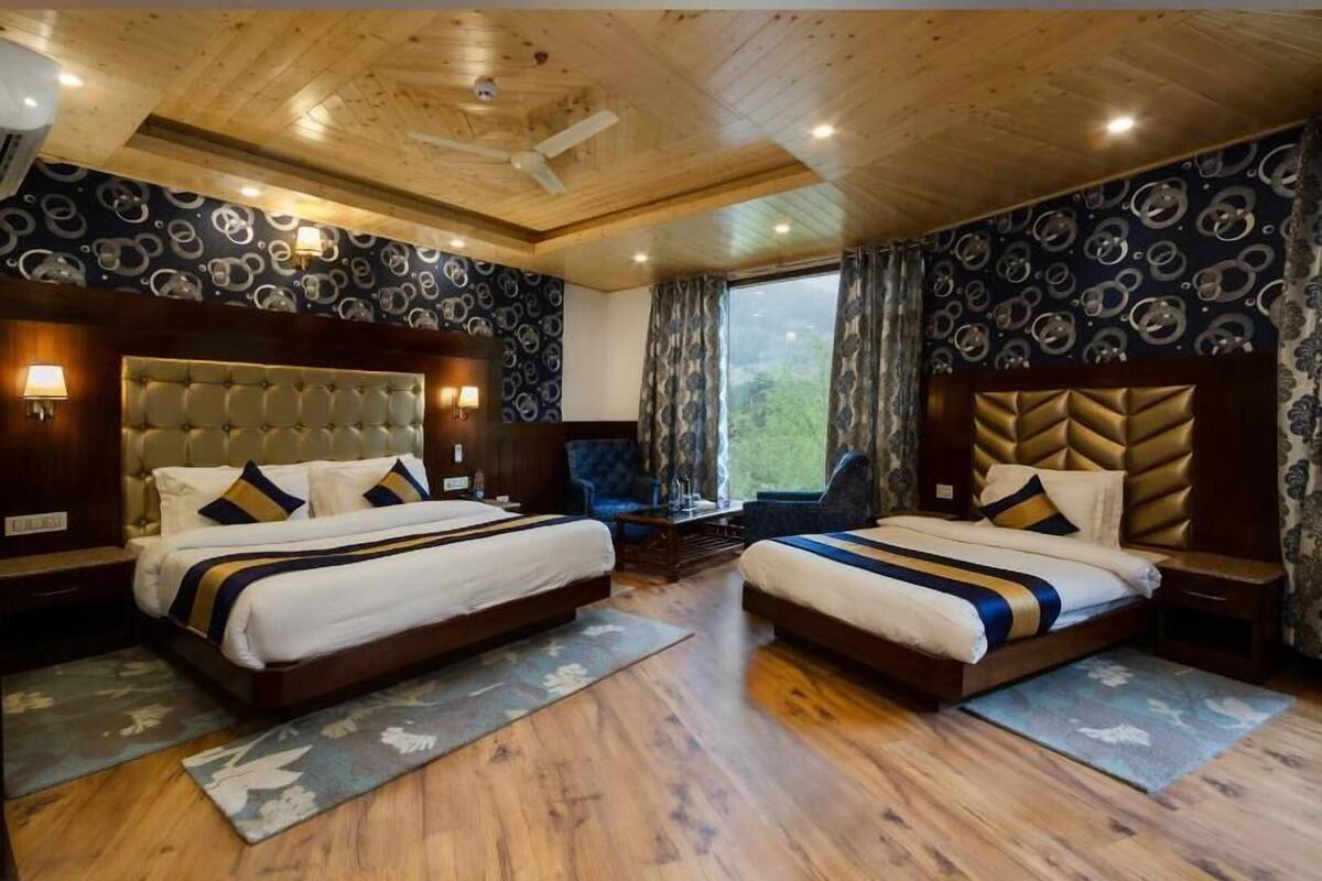 Quarto duplo com duas camas, soalho de madeira, papel de parede estampado e janela com cortinas.