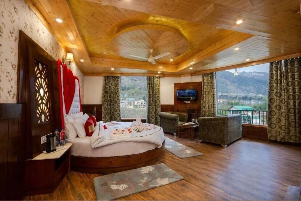 Um quarto espaçoso com uma cama grande, televisão e varanda com vista para as montanhas.