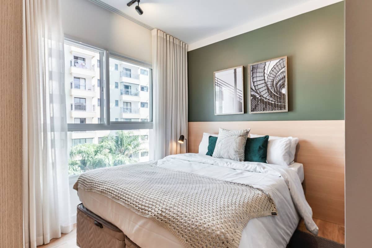 Quarto com cama grande, vista de edifícios e duas quadros na parede.