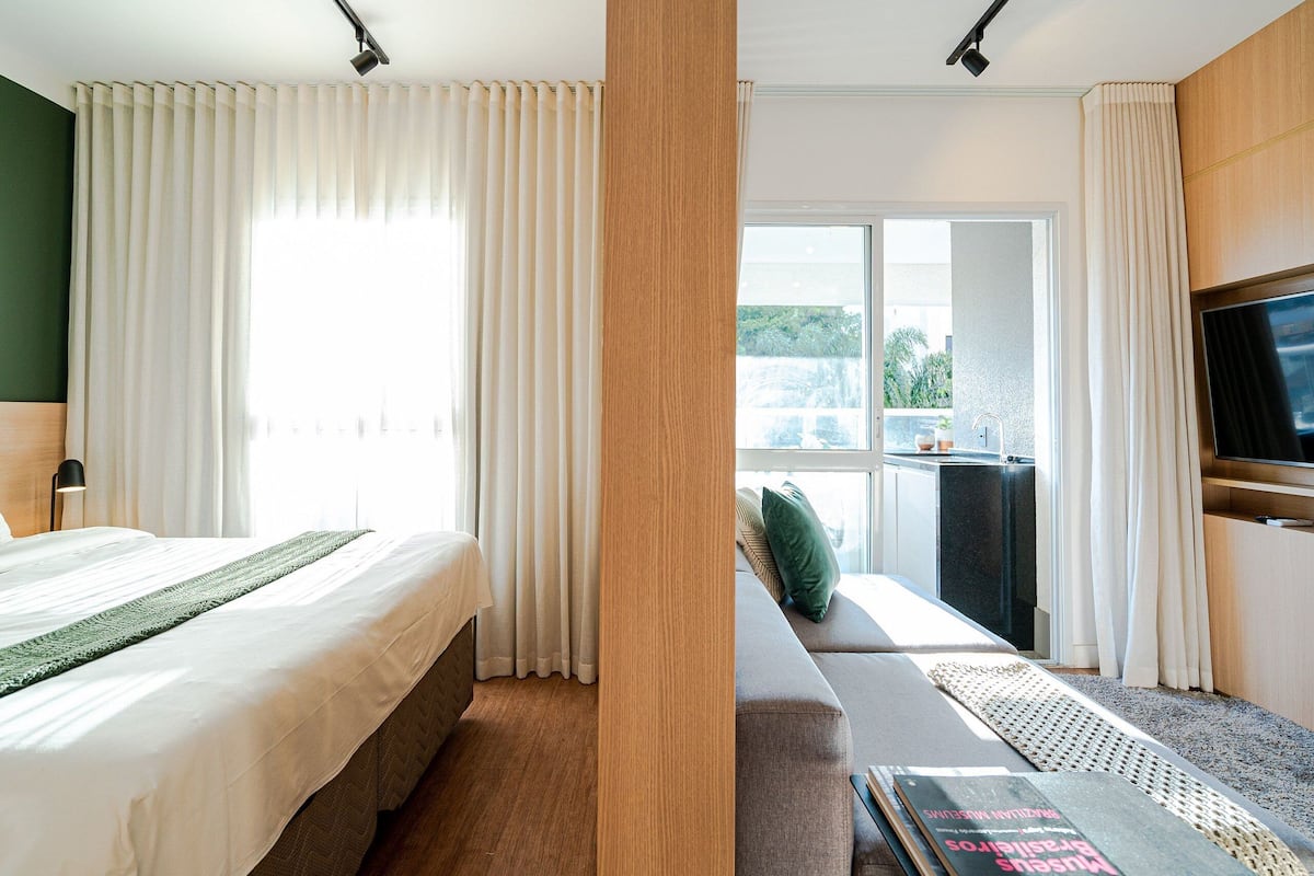 Quarto de hotel com cama, sofá, televisão e varanda com vista.