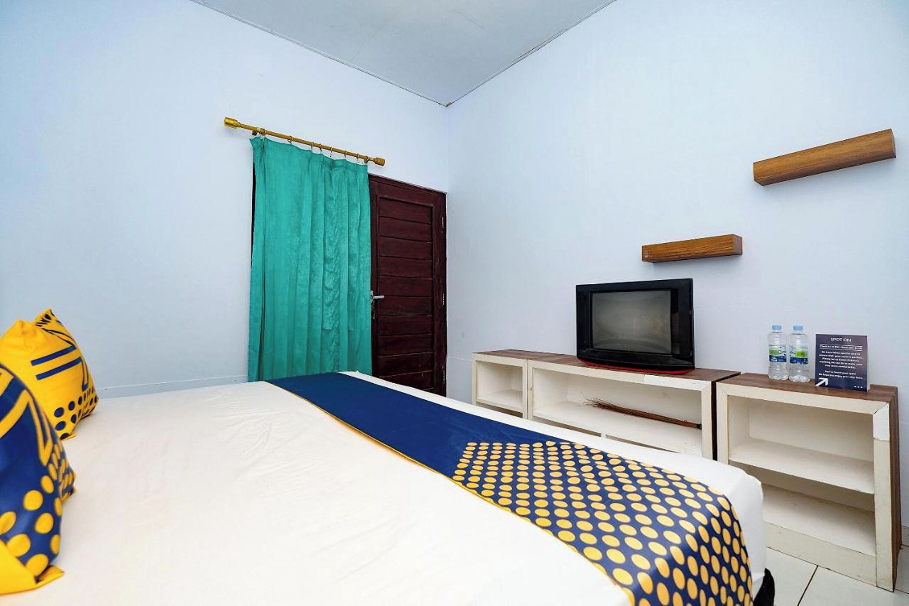 Quarto de hotel com cama, televisão, escrivaninha e armário.