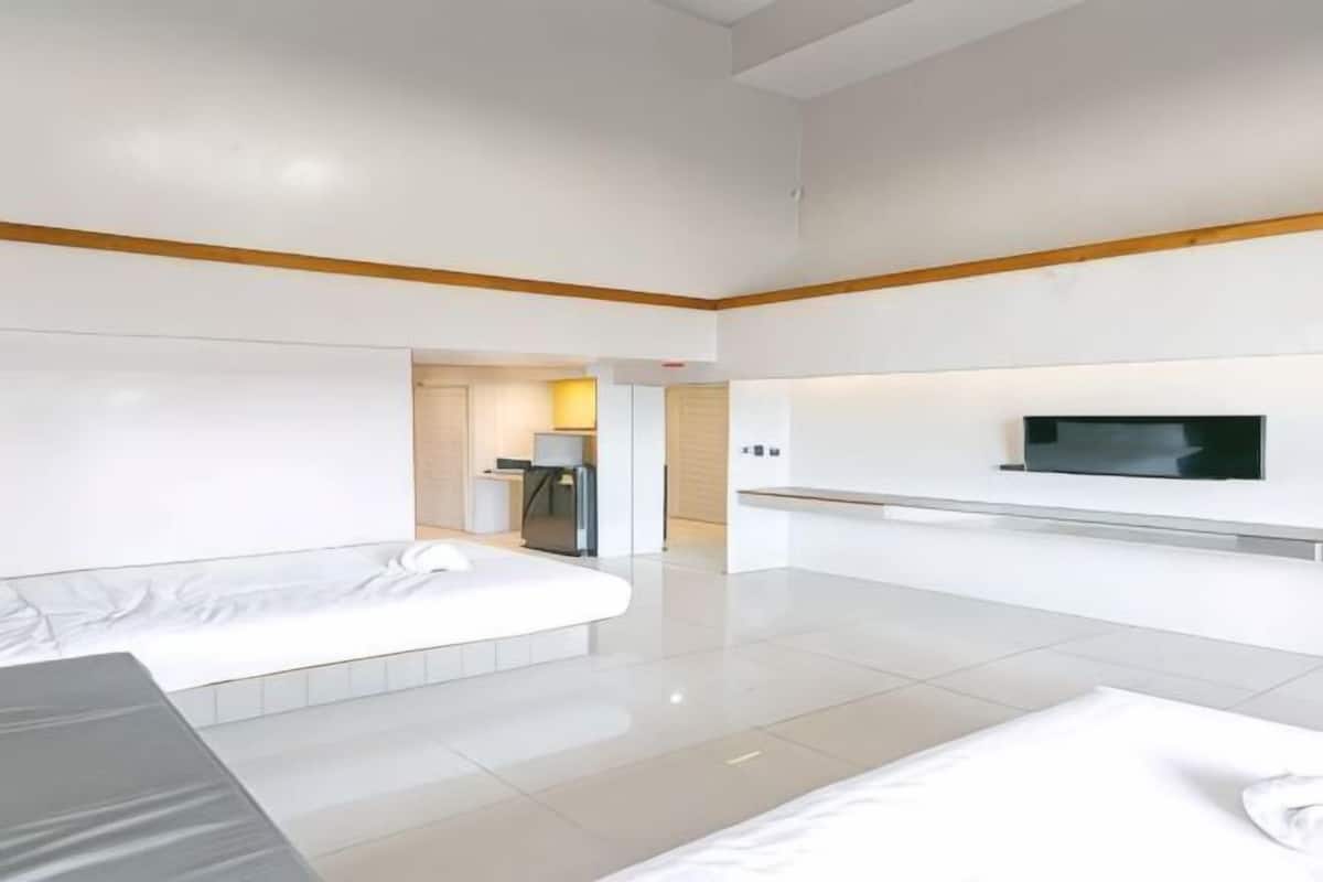 Quarto de hotel moderno com uma cama grande, televisão de tela plana na parede e uma área de cozinha compacta.