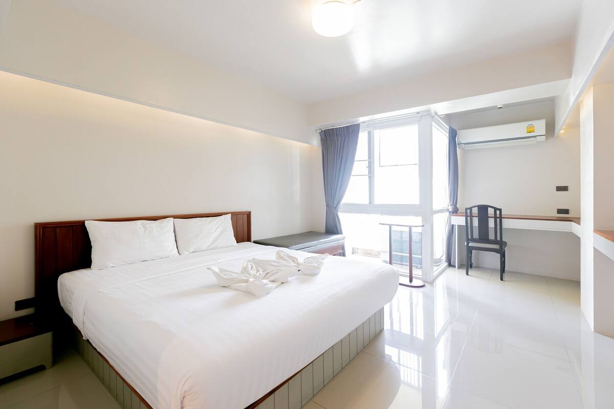 Quarto de hotel com uma cama bem arrumada, uma escrivaninha e uma cadeira.