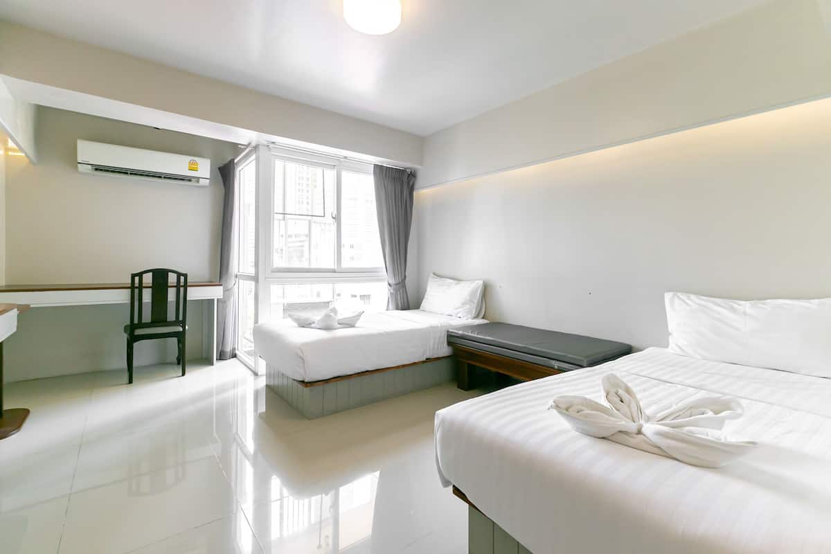 Quarto de hotel com cama, escrivaninha, cadeira e janela com cortinas.