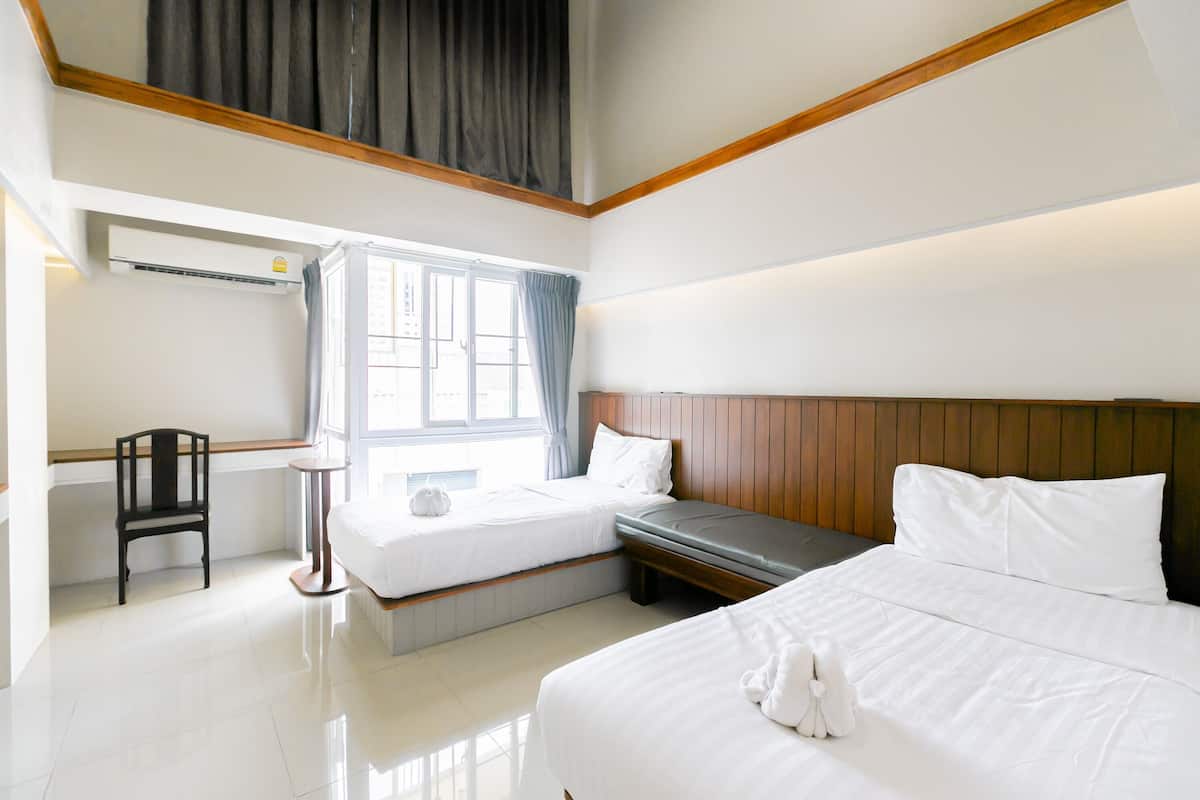 Quarto de hotel com cama, uma cadeira, uma mesa pequena e janela com cortinas.