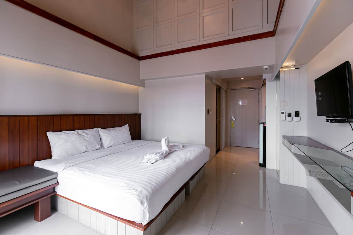 Quarto de hotel com cama, televisão, secretária e banheiro.
