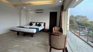 Quarto de hotel com cama, uma cadeira e varanda com vista para a rua.