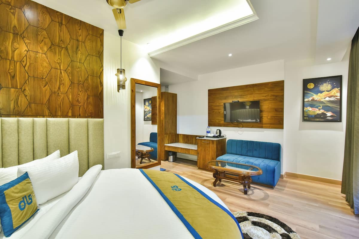 Quarto de hotel com uma cama grande, um sofá azul, um painel de parede de madeira e uma TV fixada acima do sofá.