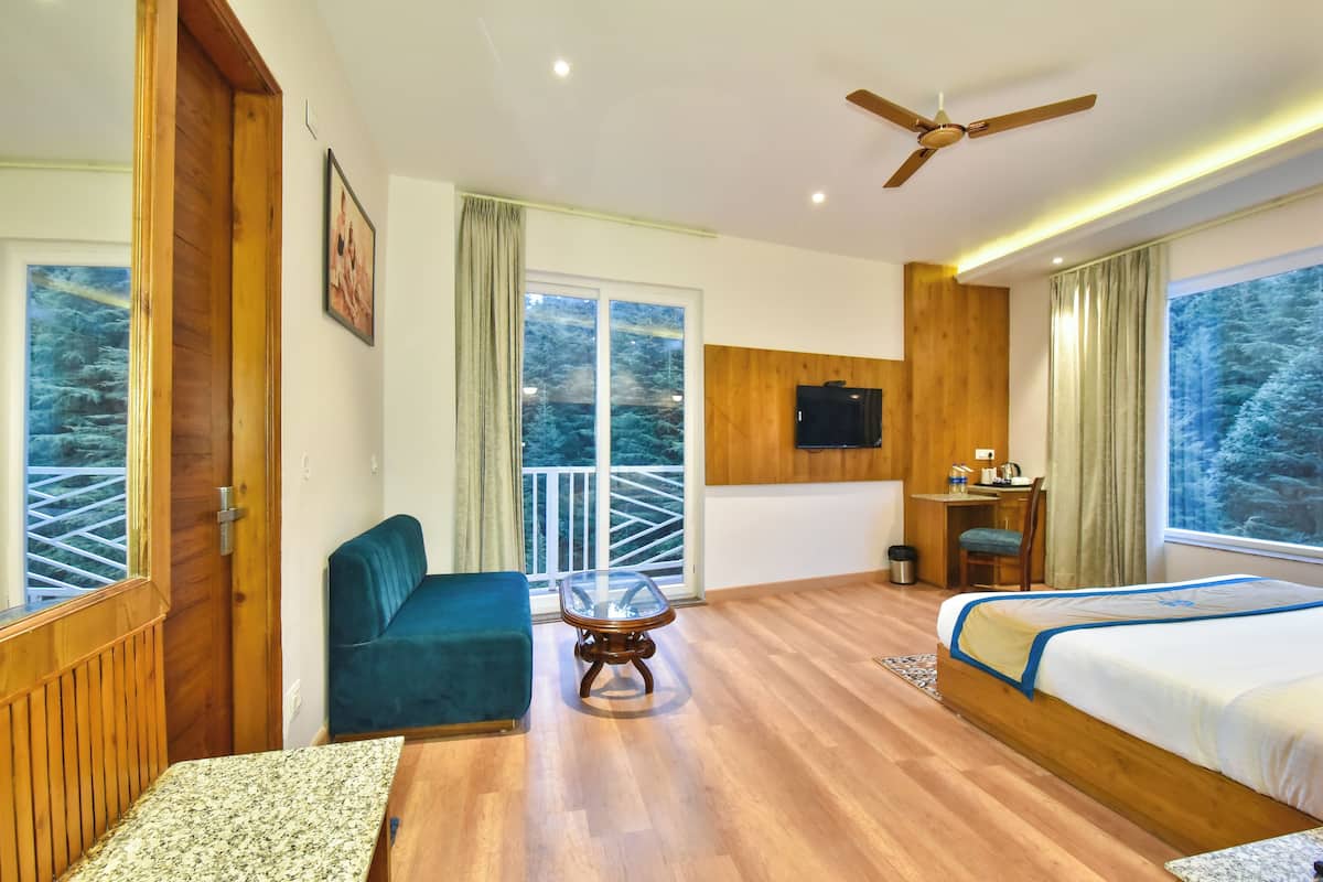 Quarto de hotel moderno com piso de madeira, uma cama, escrivaninha, poltrona, sofá e ventilador de teto.
