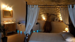 Um quarto com cama de dossel, penteadeira de madeira, espelho e mesa de cabeceira com abajur.