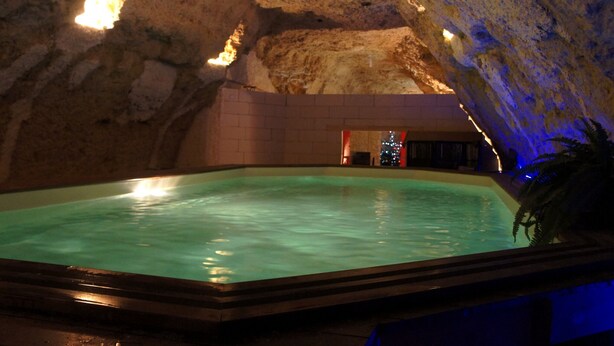 Piscina com teto em forma de gruta natural, iluminada por luzes artificiais.