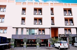 Um hotel com várias varandas, aparelhos de ar condicionado e uma placa com a inscrição "Jain's Hotel Rajhans".
