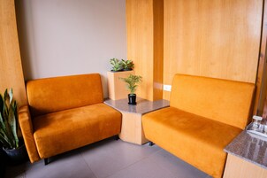 Uma área de recepção com dois sofás laranja, um balcão de madeira e um vaso de plantas.