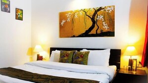 Quarto de hotel com uma cama grande, duas luminárias de cabeceira, um quadro de uma árvore florida e uma cortina vermelha.