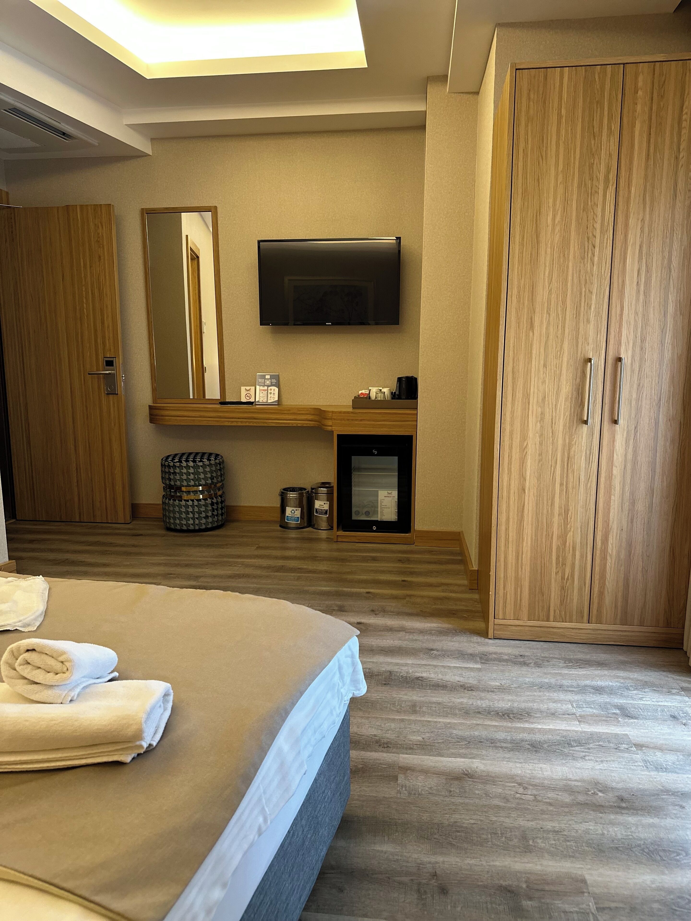 Quarto de hotel com cama, televisão na parede, minibar e guarda-roupa de madeira.