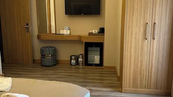 Quarto de hotel com cama, televisão na parede, minibar e guarda-roupa de madeira.