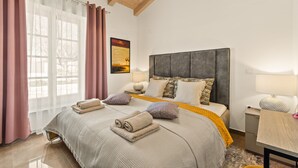 Quarto com cama grande, cabeceira, mesa de cabeceira, abajur e janela com cortinas.