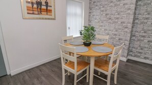 Uma área de refeições com uma mesa redonda de madeira, quatro cadeiras brancas e um vaso com planta.