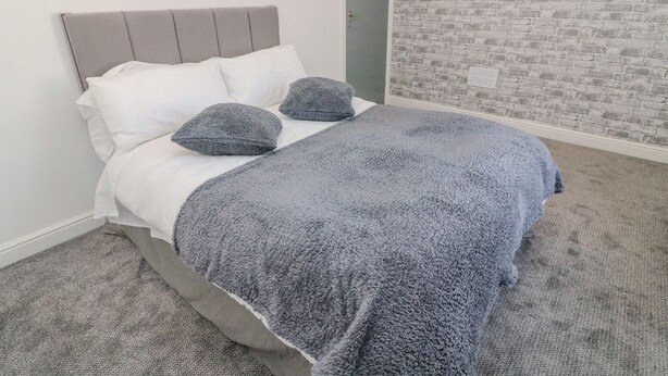 Quarto com cabeceira cinza, roupa de cama branca e manta cinza.