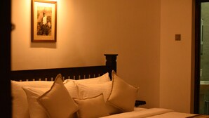 Quarto de hotel com cama, travesseiros, cabeceira, quadro na parede e uma porta.
