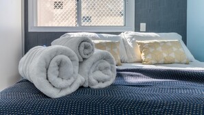 Cama bem arrumada com toalhas dobradas, manta estampada e almofadas decorativas.
