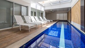 Piscina com espreguiçadeiras, claraboia e piso ladrilhado.