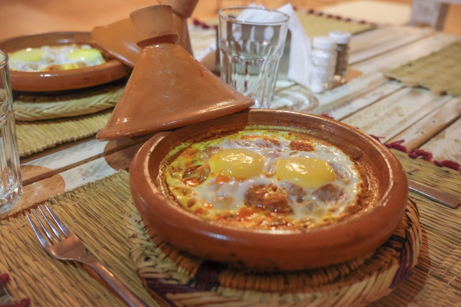 Um prato tradicional marroquino de tagine, com ovos e carne, servido em um pote de barro sobre um tapete tecido.