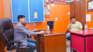 Dois homens em um escritório, com uma mesa, computador e garrafa de água.