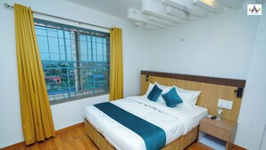 Quarto de hotel com uma cama grande, cabeceira de madeira, mesa de cabeceira e uma janela com cortinas amarelas.