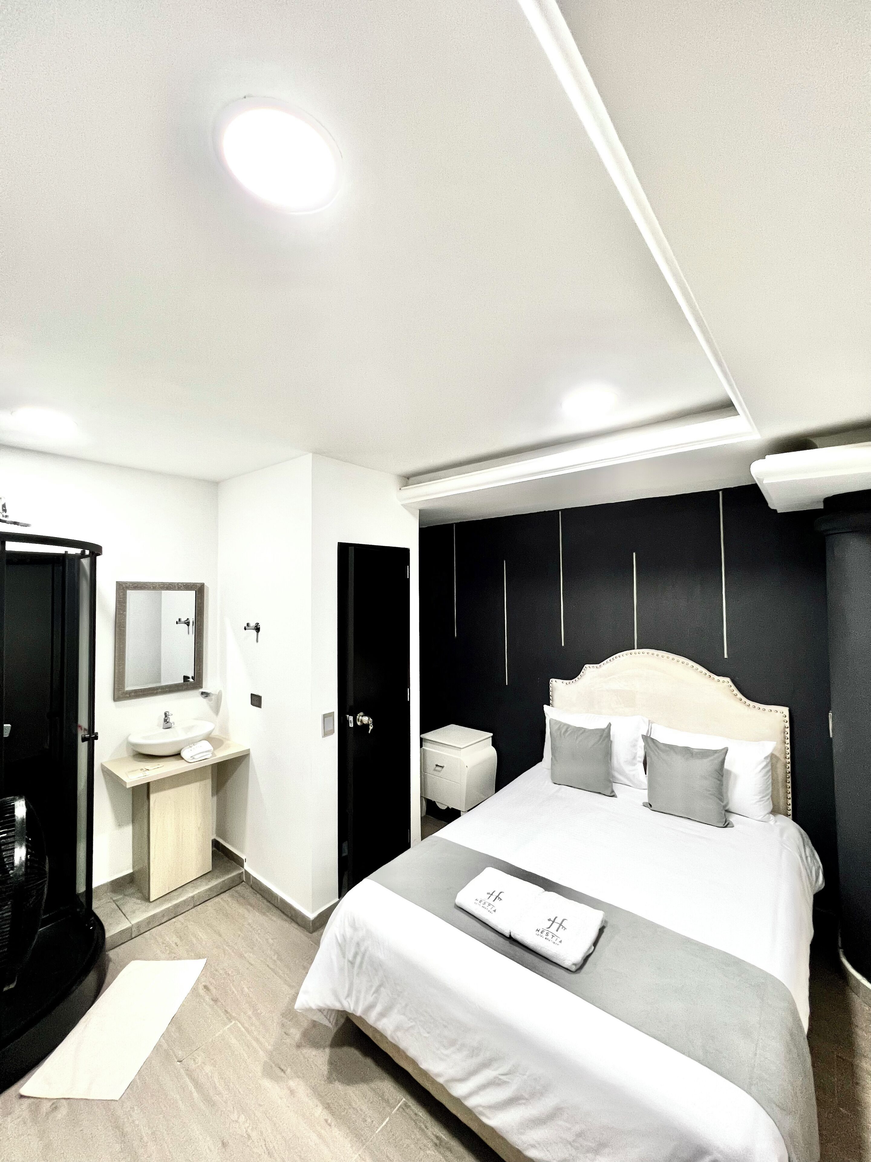 Quarto moderno com cama grande, mesas de cabeceira, roupeiro embutido, toucador com espelho e luminária no teto.