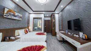Quarto de hotel com duas camas, uma mesa de trabalho com televisão e vista para a cidade.