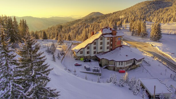 Uma cabana coberta de neve com uma pista de esqui ao fundo.