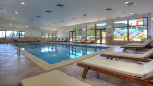Piscina interna com espreguiçadeiras e grandes janelas.