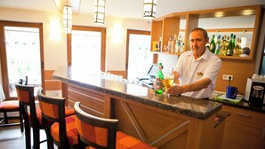 Uma área de bar com um bartender, balcão, banquetas e prateleiras com garrafas.
