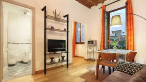Uma sala de estar com televisão, mesa de jantar com cadeiras, sofá e janela com cortinas.