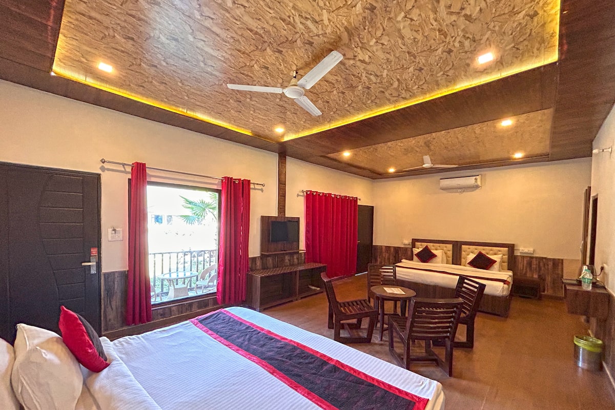 Quarto de hotel com cama, escrivaninha, cadeira, ventoinha no teto e janela com cortinas.