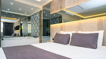 Quarto de hotel moderno com uma cama grande, área de estar separada, banheira e um espelho amplo.