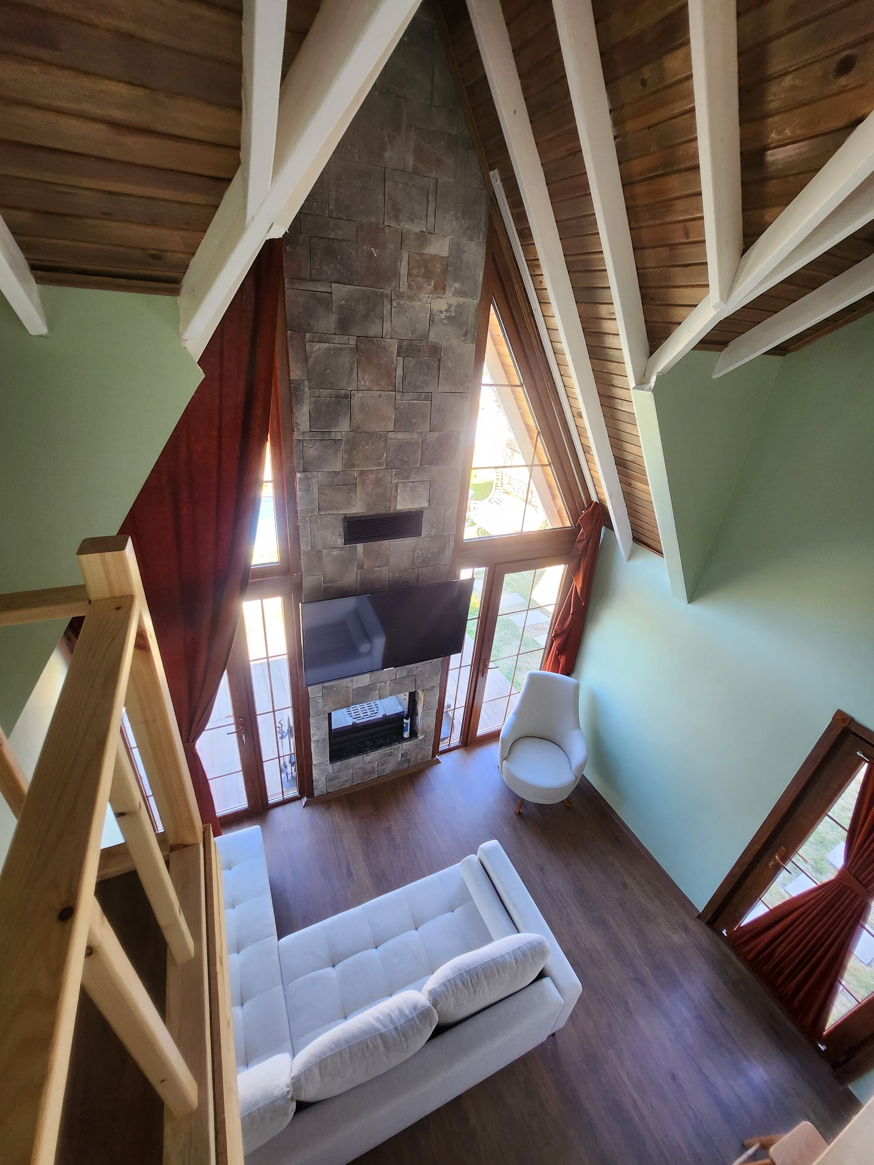 Um quarto aconchegante com lareira de pedra, um sofá branco e teto de madeira.