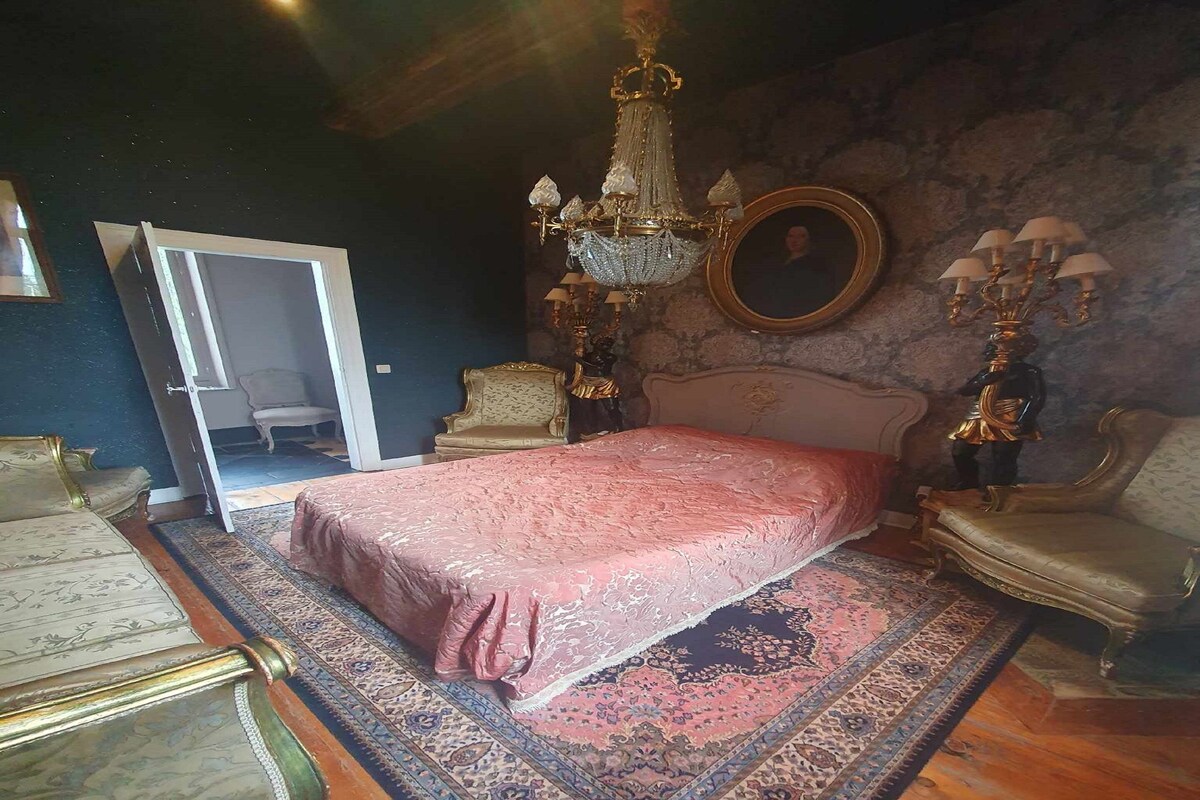 Quarto com cama grande, lustre ornamentado e móveis clássicos.