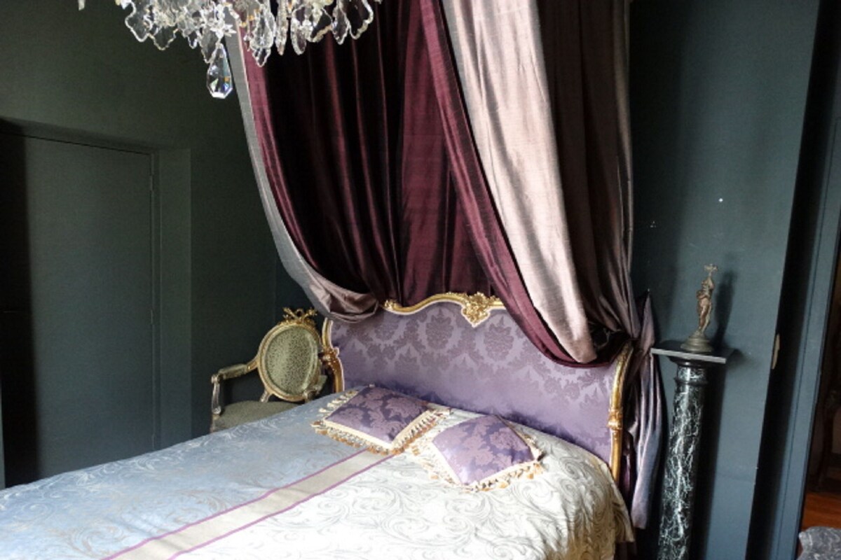 Quarto com cama de dossel, espelho, estátua e uma coluna alta.