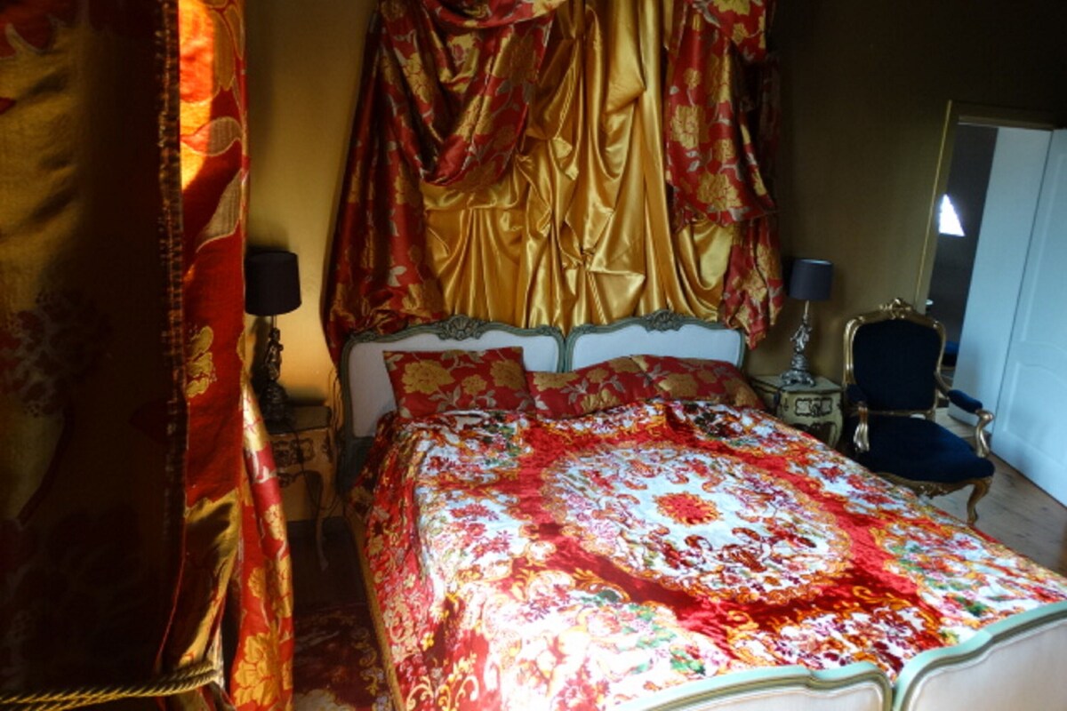Quarto com uma cama grande, mesa de cabeceira, cadeira e cortinas.