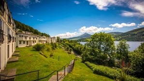Hotel com gramado, caminho de pedra e vista para um lago e montanhas.