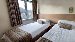 Quarto de hotel com duas camas, uma janela grande com cortinas, e vista para o exterior.