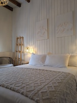 Quarto com uma cama grande, uma escada de madeira, um abajur fixado na parede e duas imagens emolduradas.