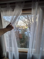Uma mão ajustando uma cortina translúcida sobre uma janela.