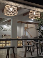 Interior de restaurante com luminárias de vime suspensas, uma escadaria e um balcão exibindo alimentos.