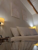 Quarto com uma cama, duas luminárias e duas obras de arte nas paredes.