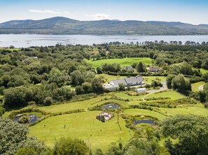 Uma grande propriedade com vários edifícios, amplos jardins verdes e um lago ao fundo.
