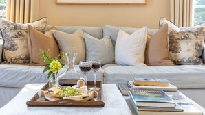 Sala de estar com sofá, bandeja de comida e bebidas, e livros sobre uma mesinha de apoio.