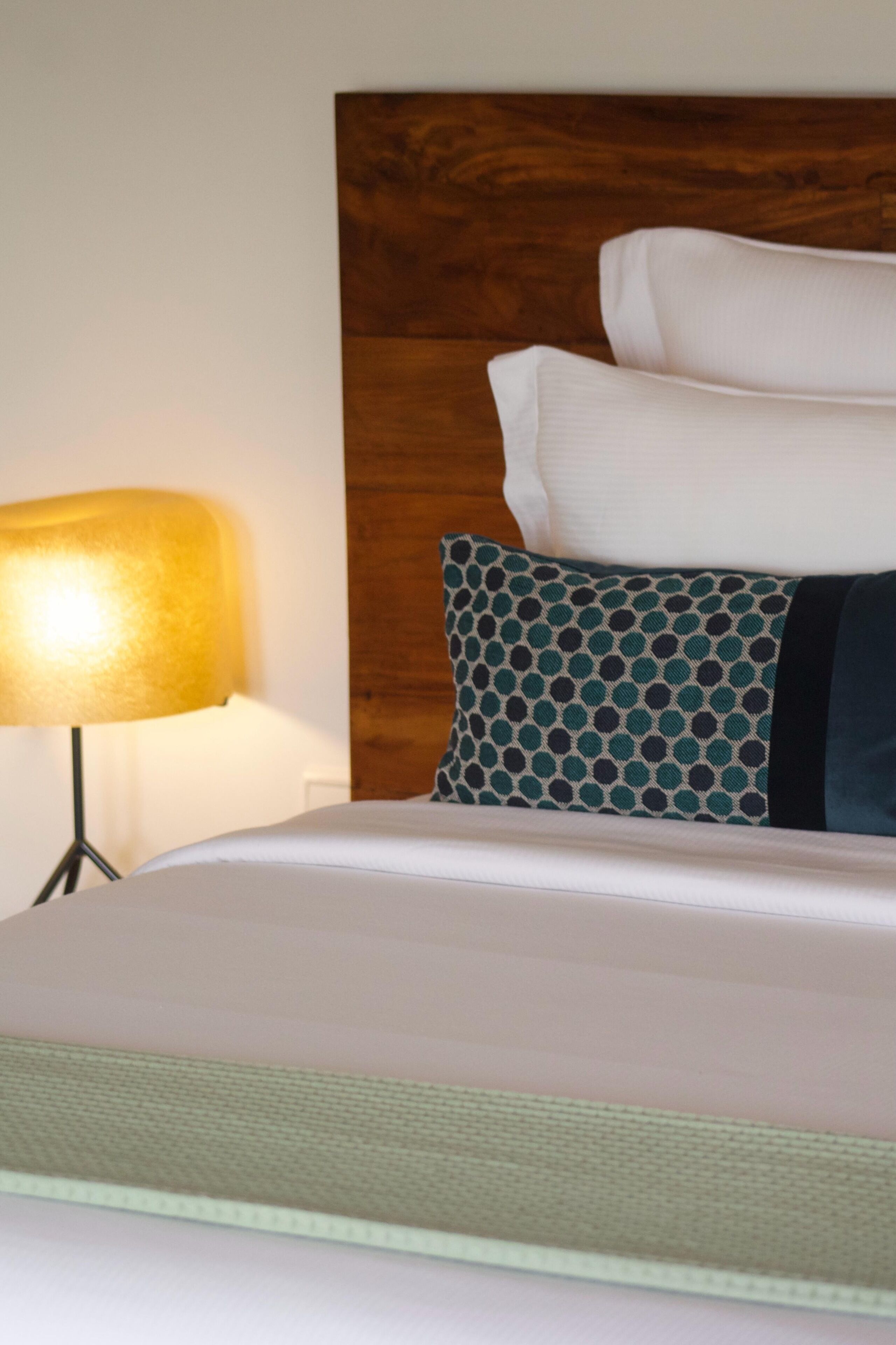 Uma cama bem arrumada com cabeceira, travesseiro estampado e abajur.